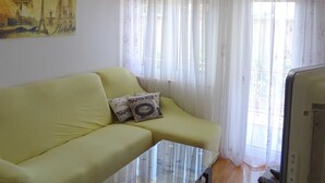 Uma sala de estar com um sofá amarelo, uma mesa de centro de vidro e um quadro com pontos turísticos de Paris na parede.