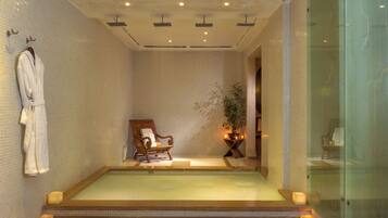 Um quarto de spa com uma banheira grande, uma cadeira de madeira e um vaso com planta.