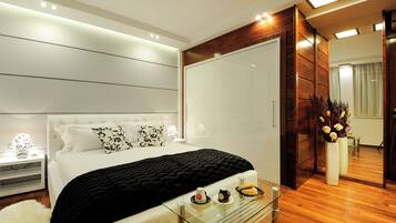 Quarto moderno com cama, mesas de cabeceira, mesa de centro de vidro e espelho.