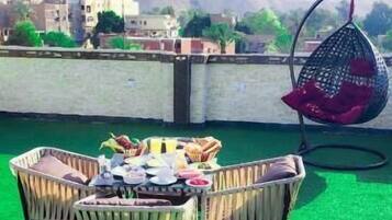 Terraço no telhado com mesa posta para refeições, uma cadeira suspensa e vista para uma pirâmide ao fundo.