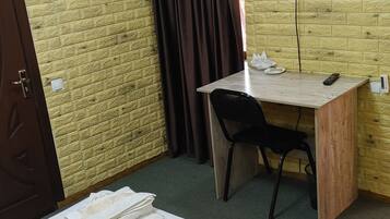 Quarto de hotel com parede em padrão de tijolos, televisão de tela plana na parede, escrivaninha de madeira com cadeira e cama com toalhas dobradas com cuidado.