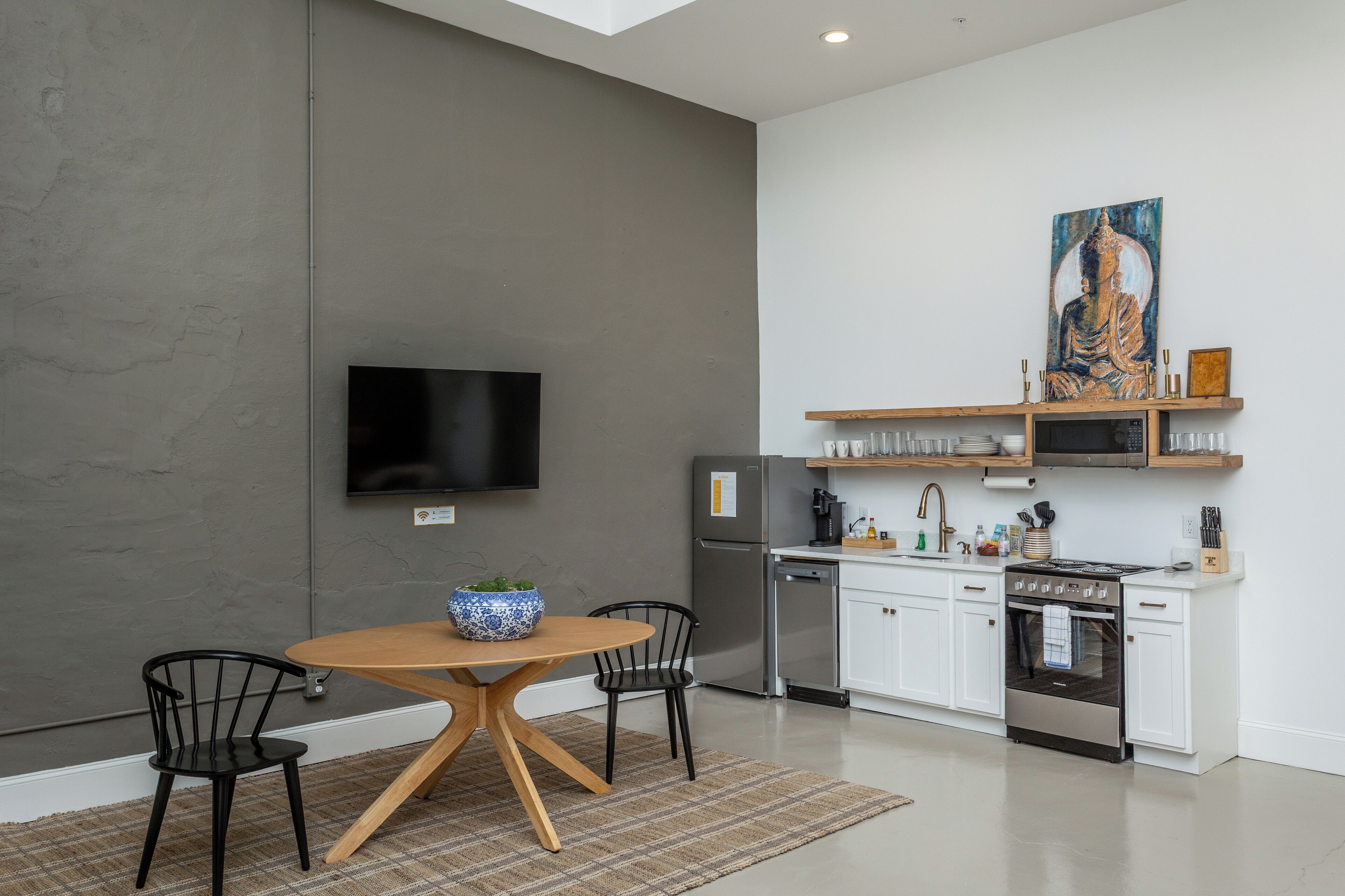 Cozinha moderna com forno embutido, geladeira e micro-ondas. Há uma mesa de jantar com cadeiras e uma TV fixada na parede.
