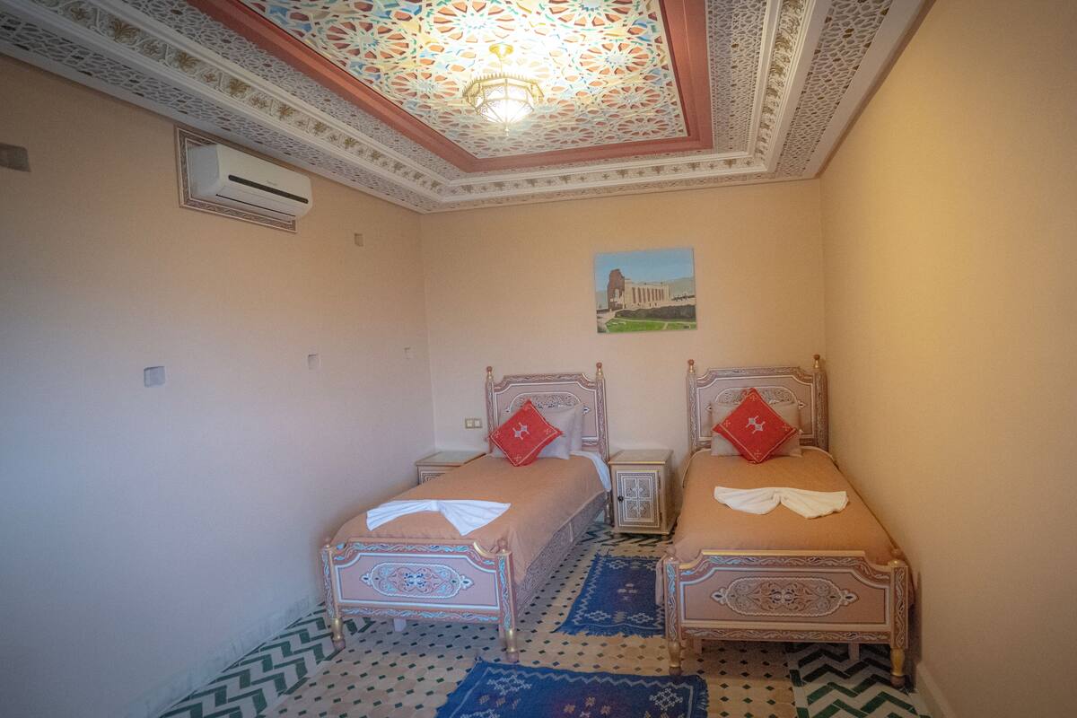 Quarto pequeno e tradicional com duas camas, tapetes estampados e teto decorativo.