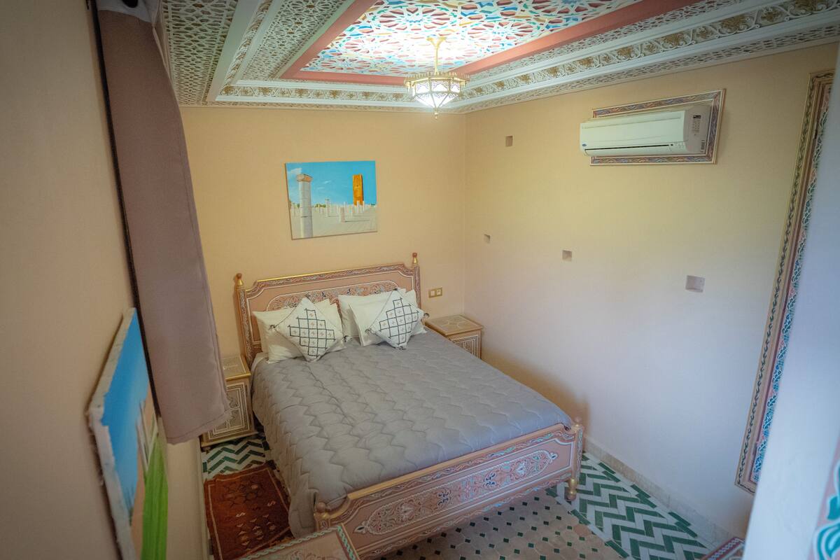 Quarto com cama, ventilador de teto, ar condicionado fixado na parede e piso estampado.