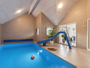 Piscina interna com um escorregador azul, uma pequena janela e um vaso de planta.