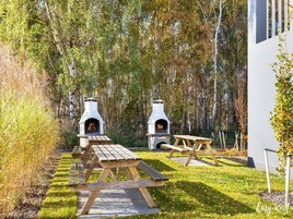 Área externa com duas fornalhas de lenha em pedra, mesas de piquenique e um gramado cercado por árvores.