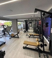 Uma academia com diversos equipamentos de exercícios, incluindo bancos e máquinas de peso, e um espelho grande que reflete o espaço.