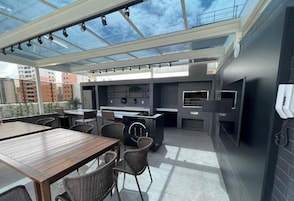 Uma área de refeições ao ar livre com teto de vidro, cozinha com eletrodomésticos modernos e vista para a cidade.