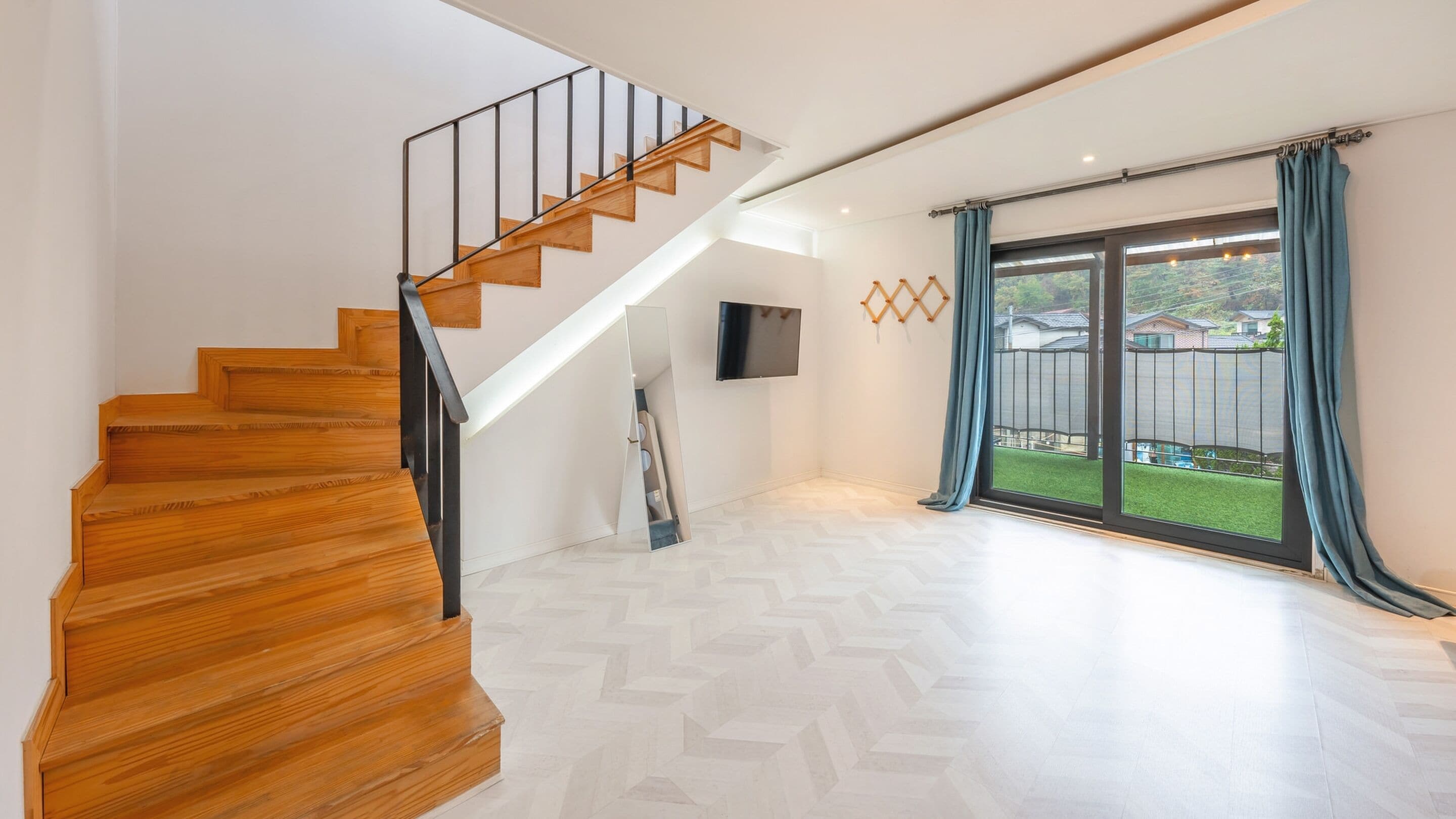 Um interior moderno com escada de madeira, TV de tela plana e uma grande porta de vidro deslizante que dá para um quintal.