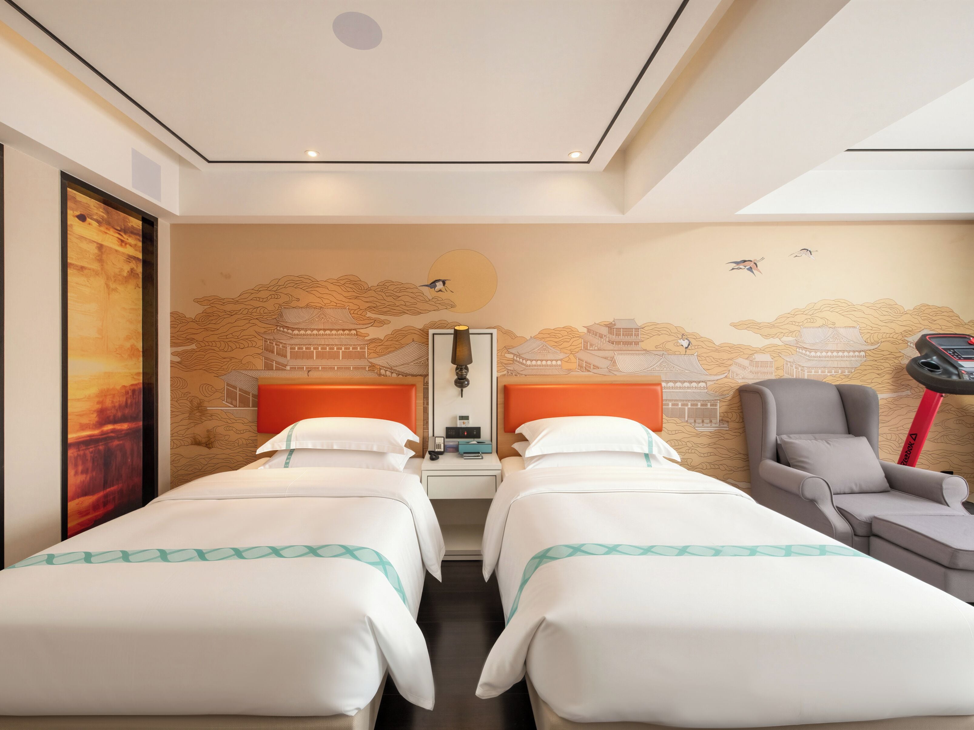 Quarto de hotel com duas camas, uma escrivaninha com luminária, uma cadeira e parede com obras de arte tradicionais.