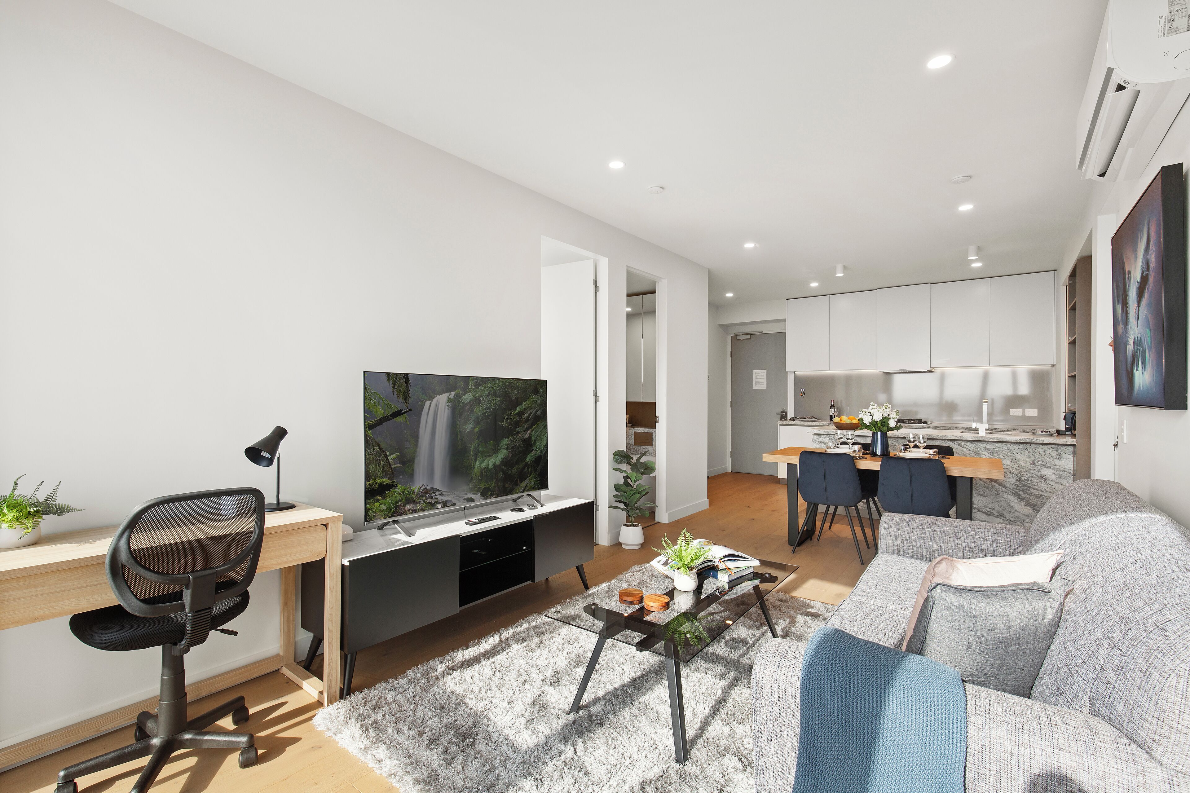 Uma sala de estar moderna com televisão, cadeira de escritório e sofá.