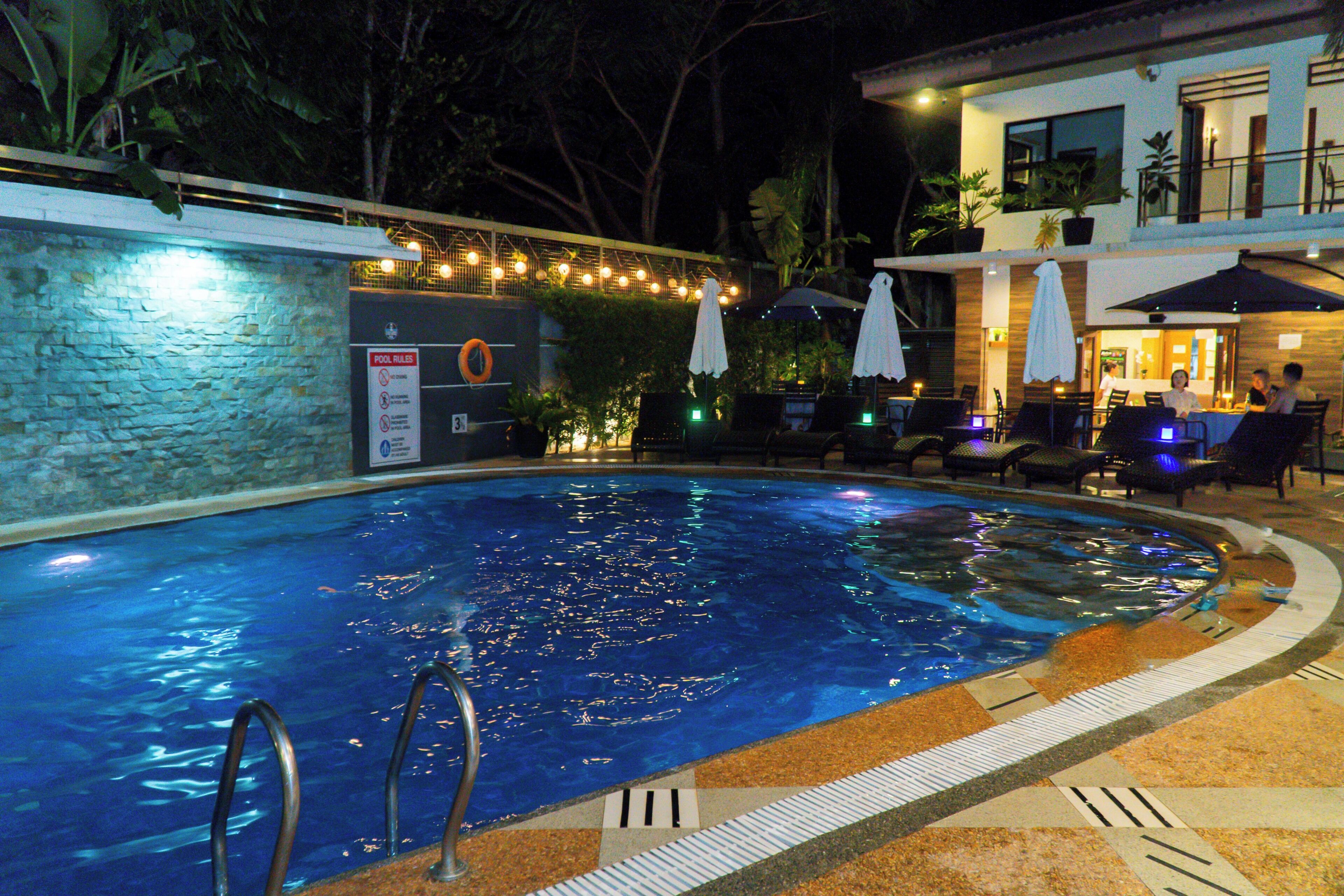 Piscina com muro de pedra e placa de sinalização, rodeada por espreguiçadeiras e guarda-sóis.