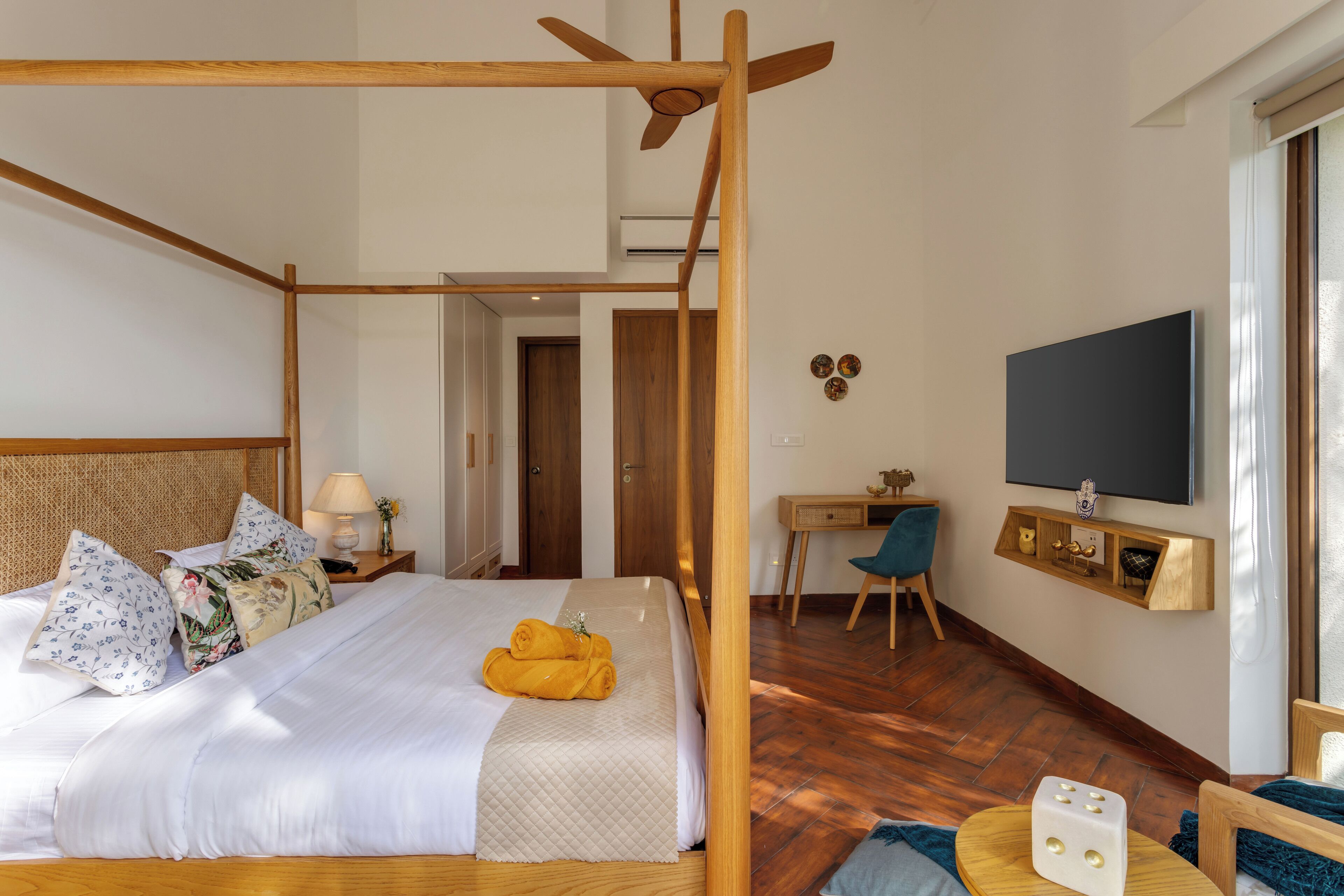 Quarto com uma cama de dossel, uma escrivaninha, uma cadeira, uma televisão e piso de madeira.