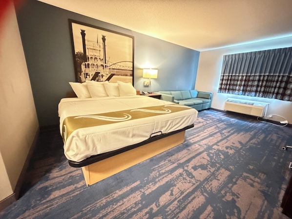 Quarto de hotel com cama grande, sofá, janela com cortinas e ar condicionado fixado na parede.