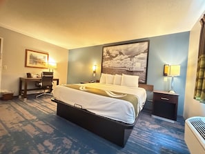Quarto de hotel com cama, escrivaninha, cadeira e uma grande pintura na parede.