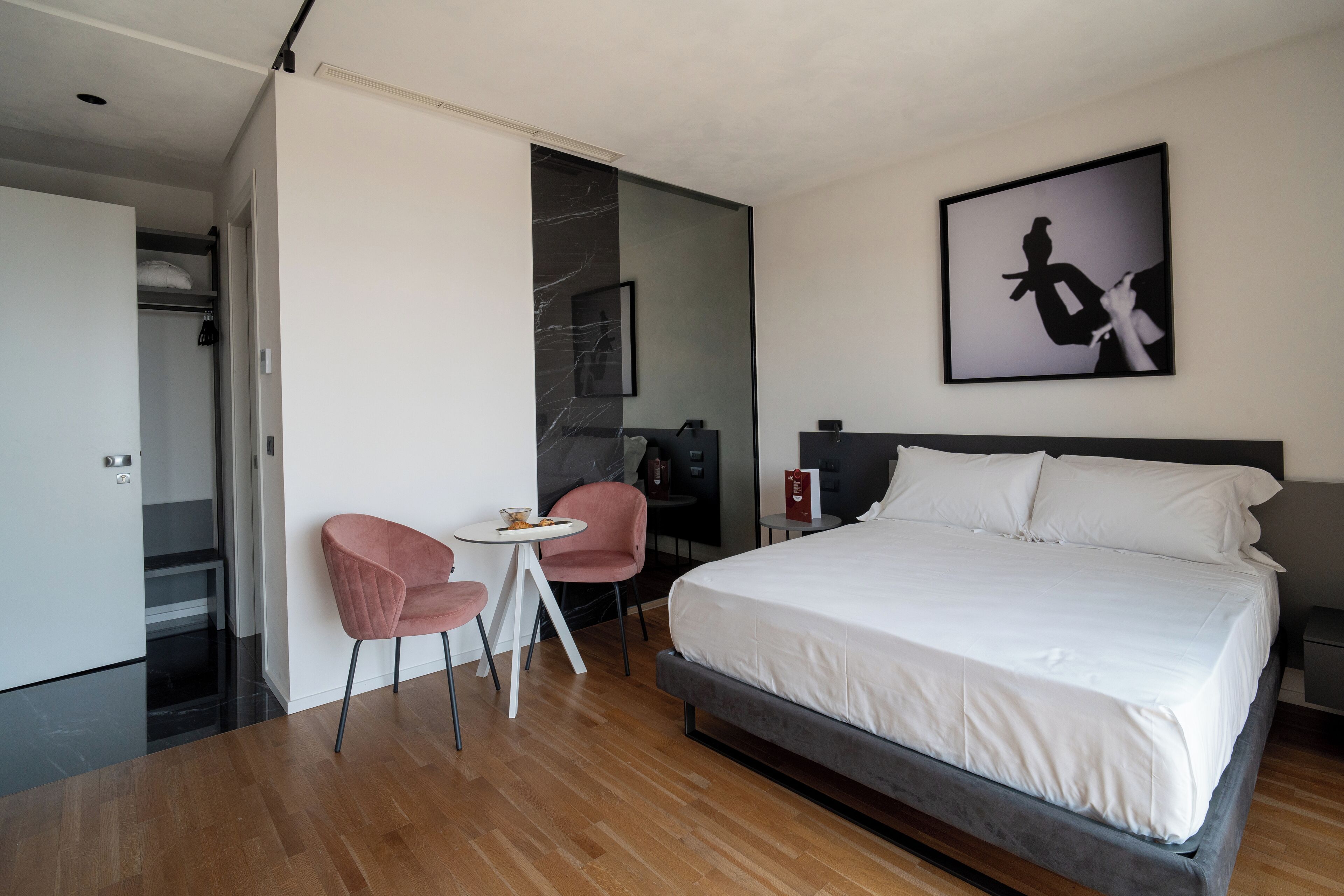 Quarto moderno com uma cama grande, uma escrivaninha pequena, duas cadeiras e uma obra de arte na parede.