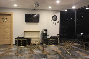 Uma área de estar moderna com televisão de tela plana, máquina de café e um letreiro com a frase 'Music Please'.