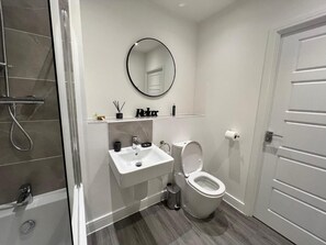 Uma casa de banho moderna com chuveiro, lavatório, sanita e espelho.