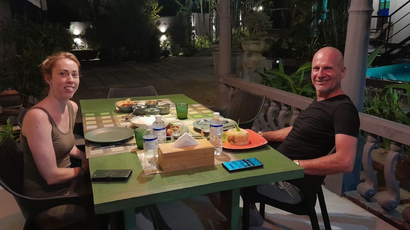 Mesa de jantar posta ao ar livre com vários pratos, um smartphone e uma garrafa de água.