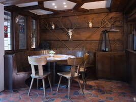 Um interior rústico de madeira com uma mesa redonda e quatro cadeiras, piso de azulejos e vigas de madeira no teto.
