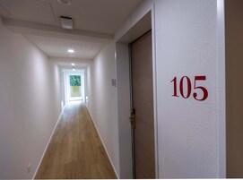 Corredor com piso de madeira, paredes brancas e porta com o número 105.