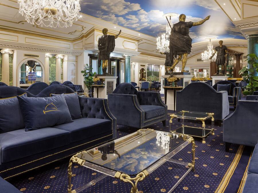 Um hall de hotel luxuoso com assentos acolchoados, lustres ornamentados e estátuas clássicas.