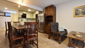 Uma sala de jantar com cadeiras de madeira e uma mesa, um sofá e uma pequena mesa com objetos decorativos.