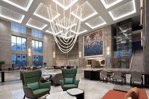 Um hall amplo com poltronas modernas verdes, um lustre grande e um teto alto com claraboias.