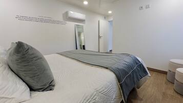 Quarto com cama, almofadas, mesa de cabeceira, espelho e porta para outro cômodo.