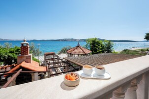 Uma varanda com vista para o mar, uma cesta de frutas e duas xícaras de café em um suporte.