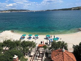 Uma praia com águas turquesa cristalinas, areal arenoso e vários guarda-sóis e espreguiçadeiras.