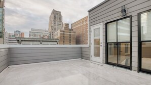 Terraço no telhado com vista para a cidade, porta de vidro deslizante e guarda-corpo de metal.