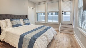 Quarto com uma cama grande, janela com persianas e escada que leva a um andar superior.