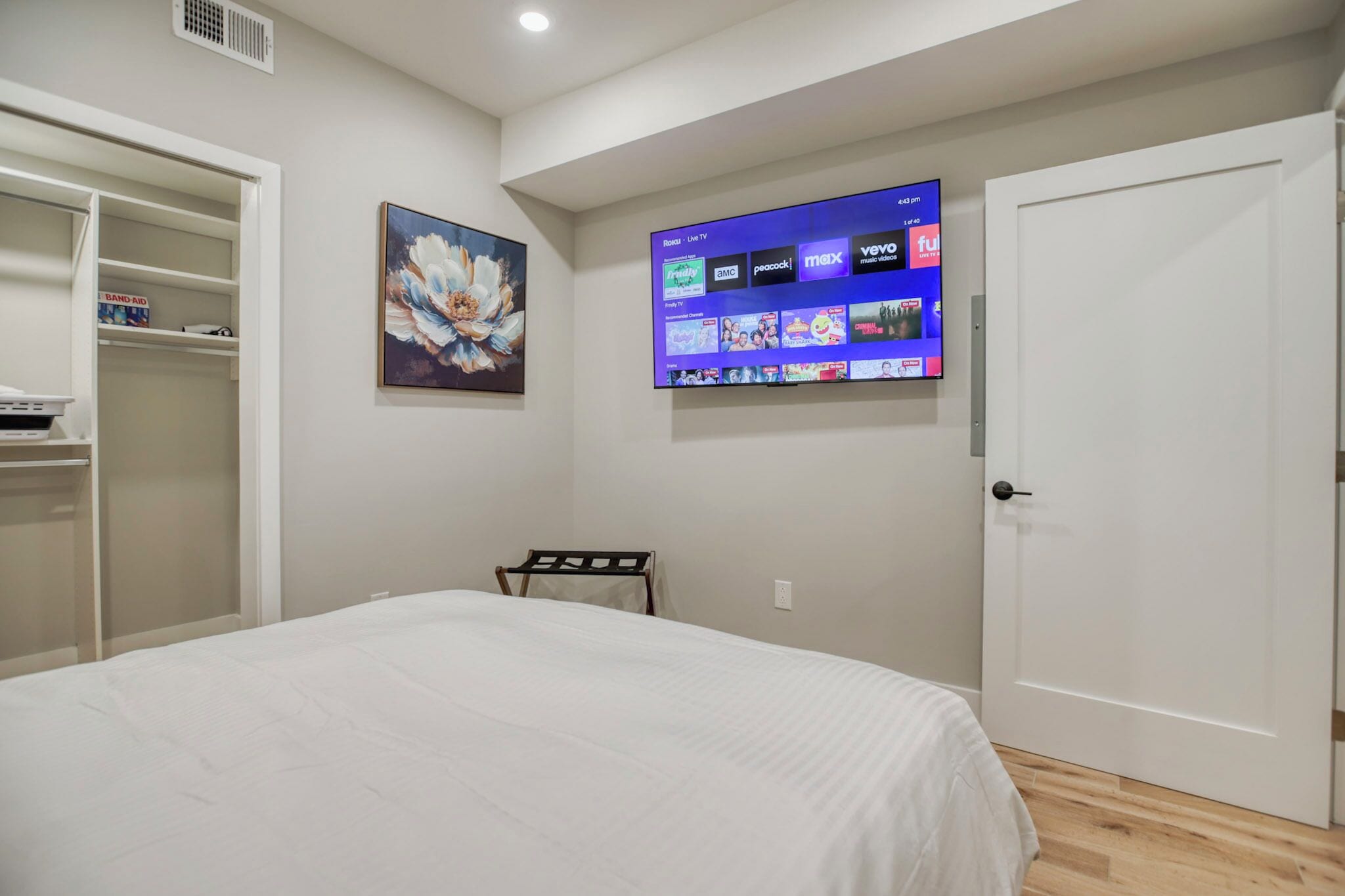 Quarto com cama, guarda-roupa, pintura e televisão com acesso a serviços de streaming.