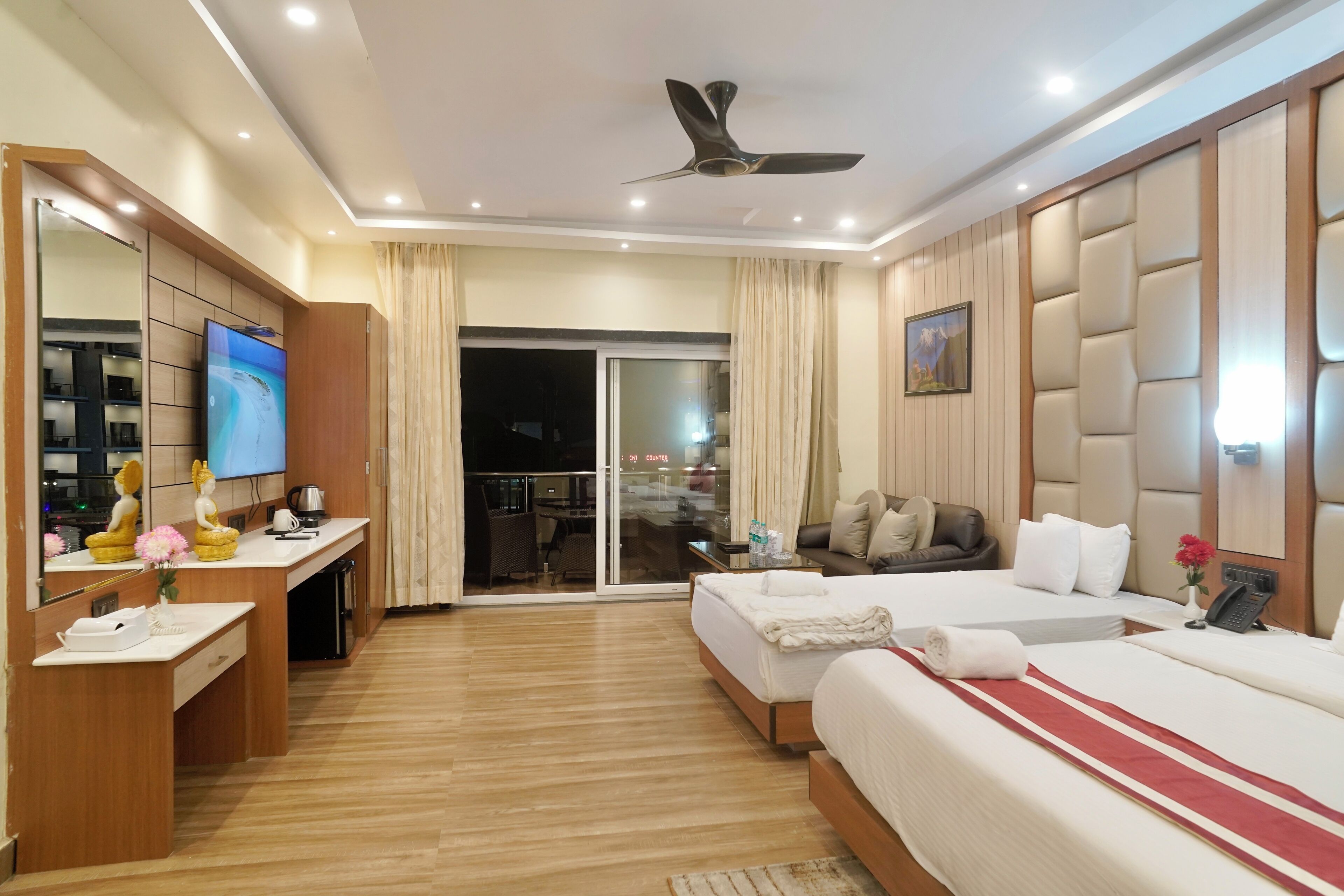 Quarto de hotel com uma cama grande, uma escrivaninha, uma televisão e uma porta de correr para uma varanda.