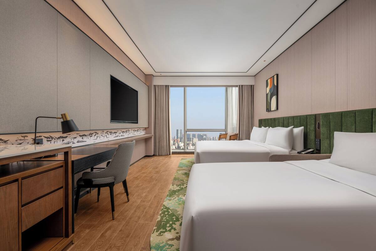 Quarto de hotel com escrivaninha, duas camas, televisão e vista para a cidade.