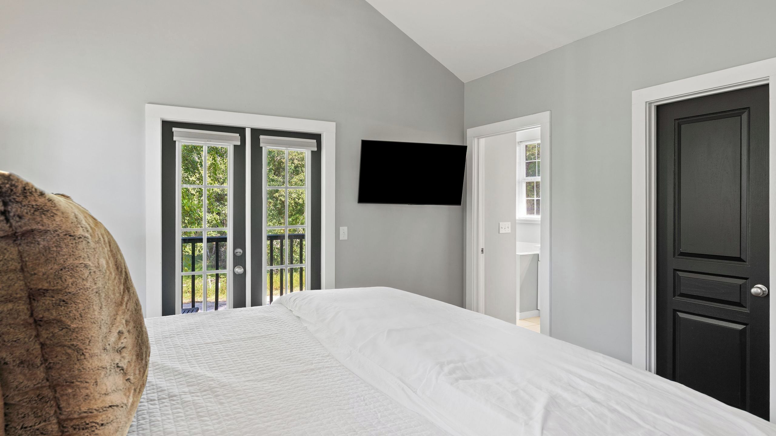 Quarto com cama, televisão presa na parede e porta que dá para uma varanda.