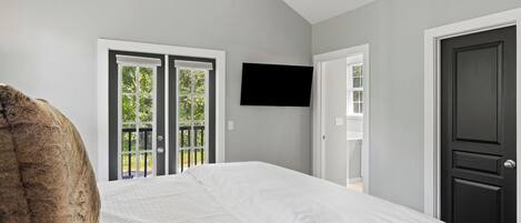 Quarto com cama, televisão presa na parede e porta que dá para uma varanda.