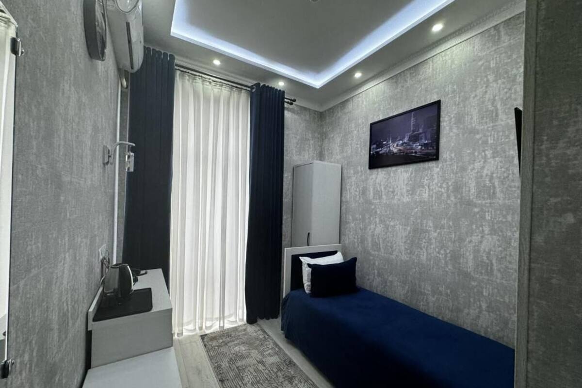 Quarto de hotel moderno com pia embutida, uma cama, uma janela grande com cortinas e uma pintura de paisagem urbana na parede.