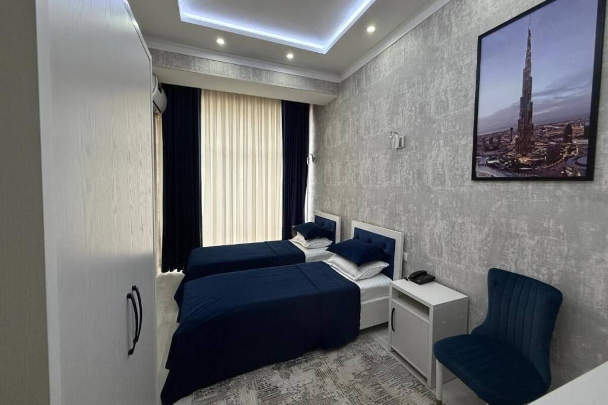 Quarto de hotel com duas camas, uma escrivaninha, uma cadeira, um quadro com vista urbana e um design de teto moderno.