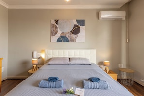 Quarto de hotel com cama, duas luminárias laterais, ar condicionado fixado na parede e um quadro.