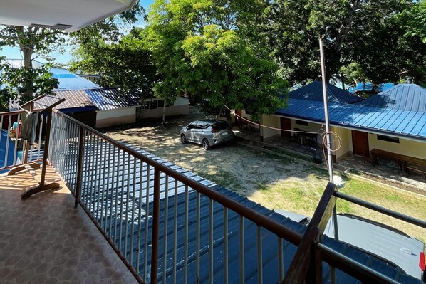 Varanda com guarda-corpo de metal com vista para um pátio onde um carro está estacionado sob uma árvore.