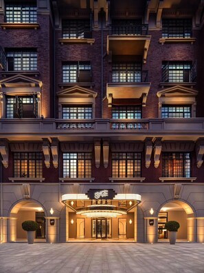 Um hotel com vários andares, uma entrada imponente com uma marquise, janelas amplas e colunas decorativas.