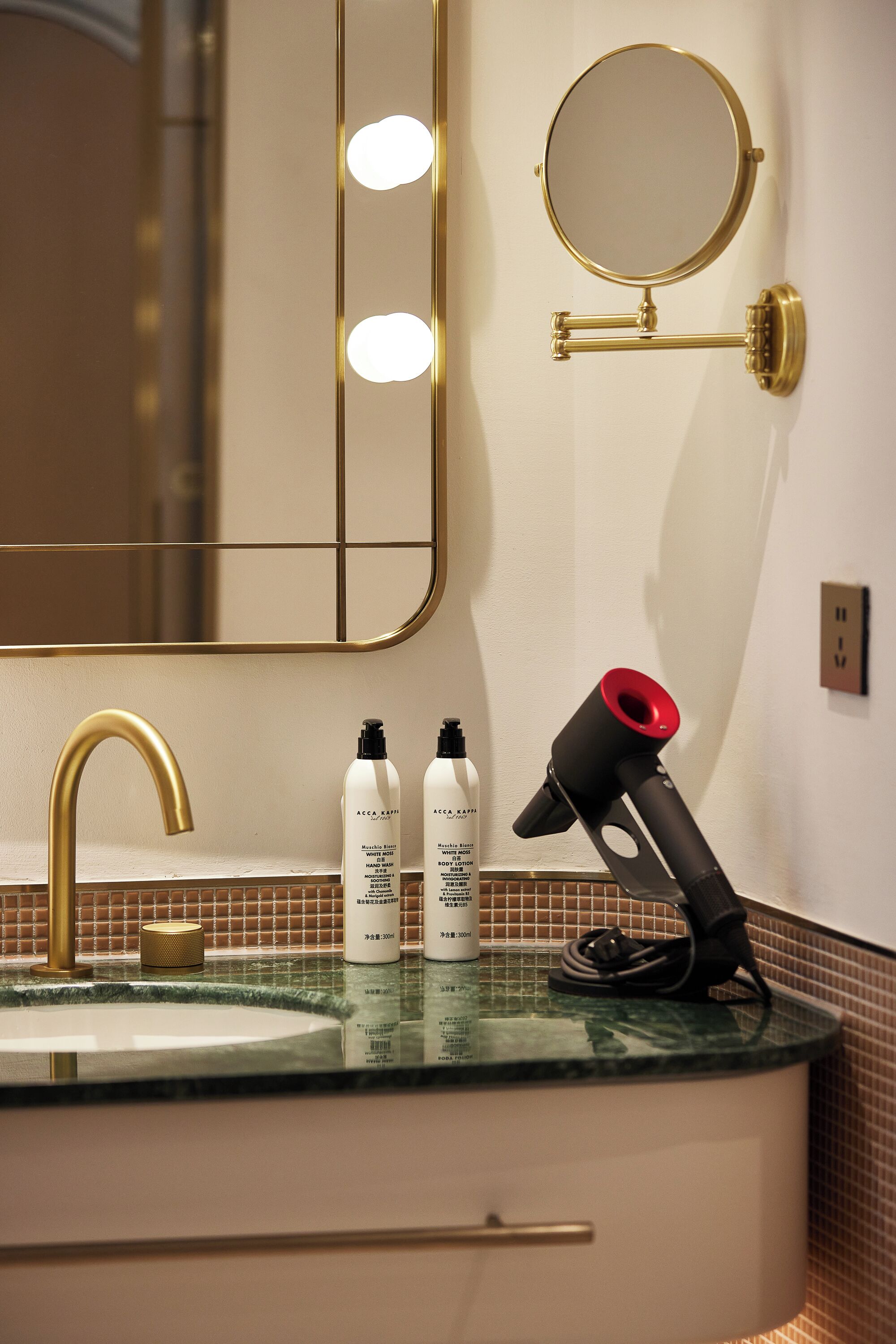 Casa de banho com torneira dourada, espelho redondo com luzes e secador de cabelo na bancada.