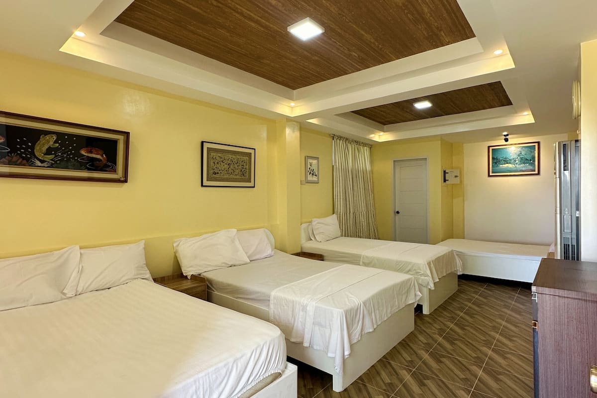 Quarto de hotel com três camas de solteiro, vigas de madeira no teto e piso de azulejos.