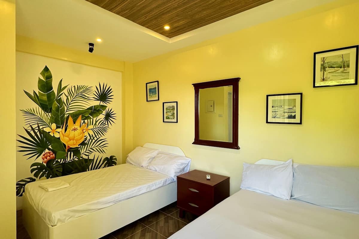 Quarto de hotel com duas camas, teto de madeira e uma grande planta tropical.
