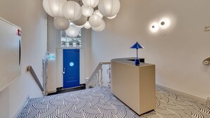 Uma área de recepção moderna com uma porta azul, piso estampado e um balcão de atendimento com luminária azul.