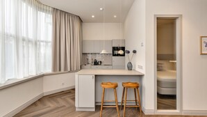Cozinha moderna com uma ilha central, dois banquetas de madeira e vista para um quarto através de uma porta aberta.