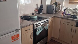 Cozinha com frigorífico branco, fogão e micro-ondas. Tem uma janela com persianas e um ventilador de teto branco.