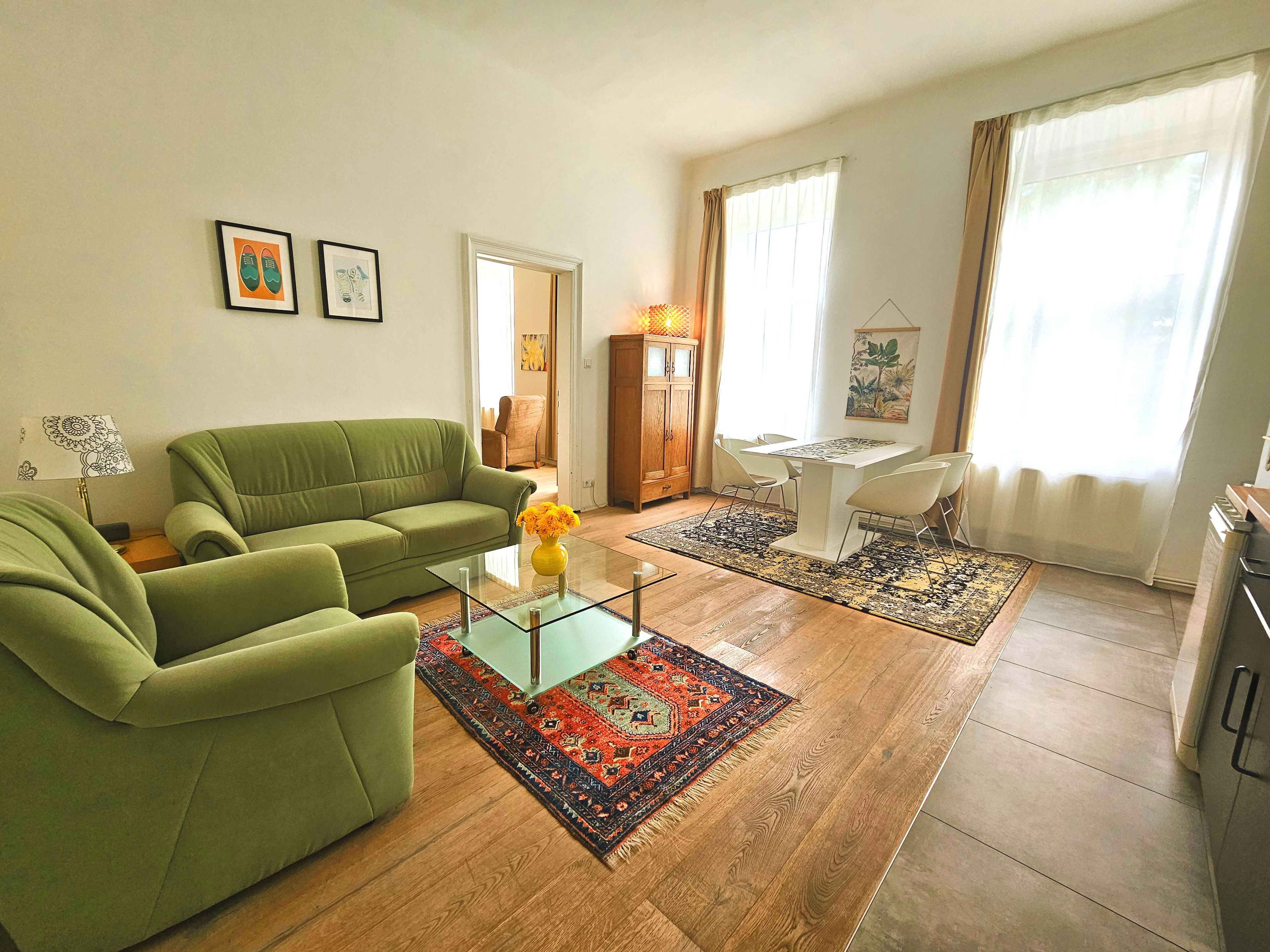 Uma sala de estar com um sofá verde, uma mesa de centro de vidro e um tapete estampado.